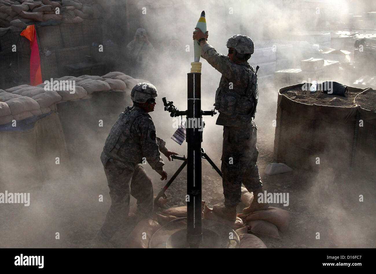 A US Army Soldier drops a 120mm mortar round into the tube while during ...