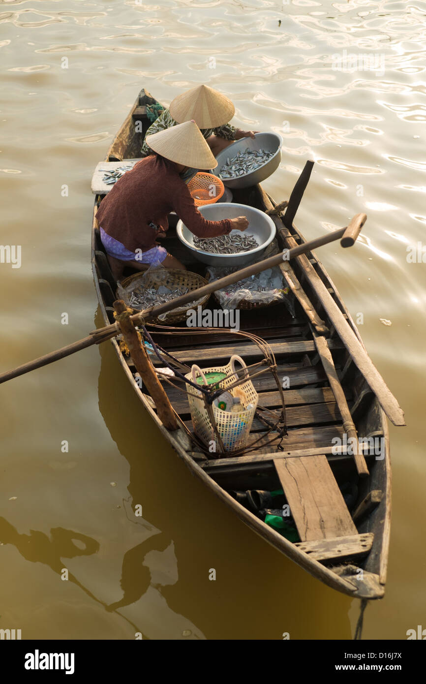 Two Vietnamese women in a traditional boat sifting through catch ...