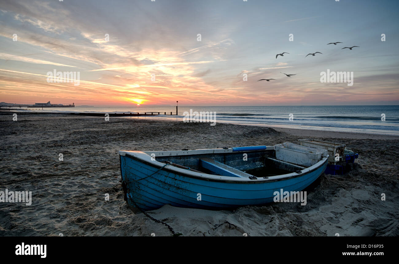 Turquoise blue fishing boat on a beach at sunrise with Bournemouth pier ...