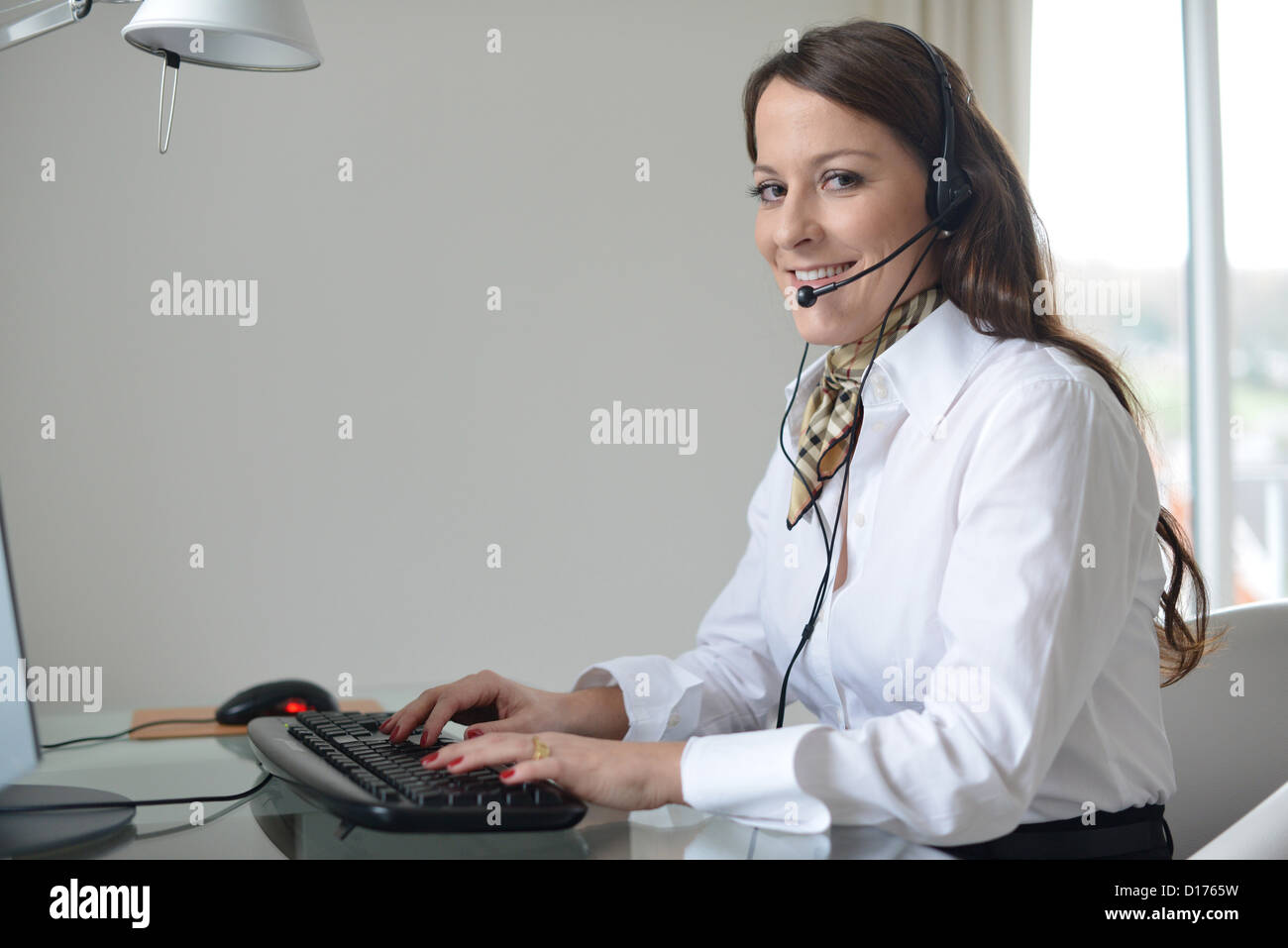 A young businesswoman is working at her computer and phoning with her ...