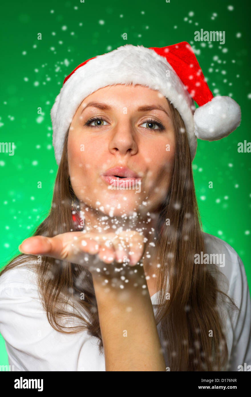 Girl in a Christmas hat blows off snowflakes on green background Stock ...