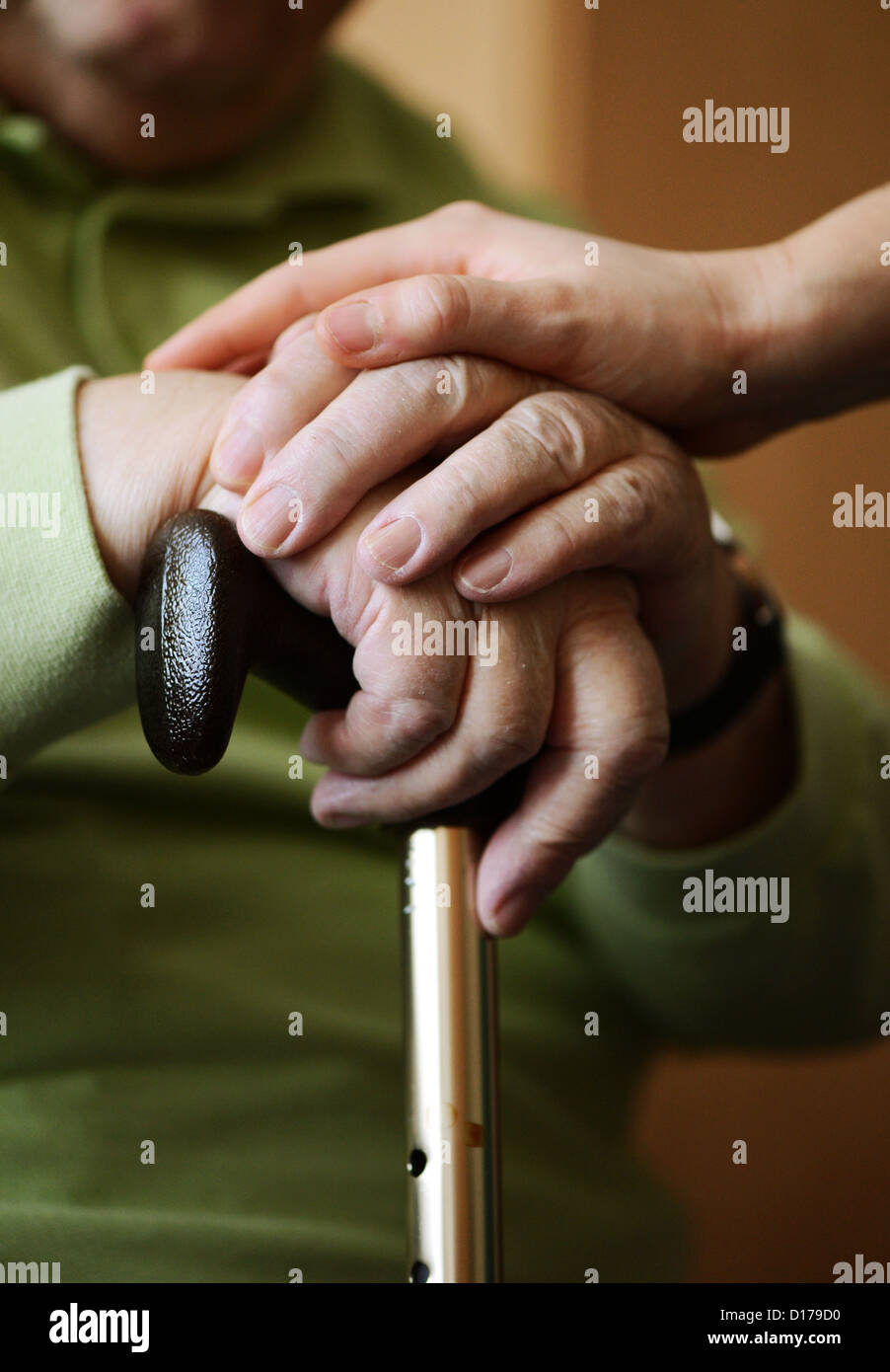 The hand of a younger person rests gently on the hands of an elderly ...