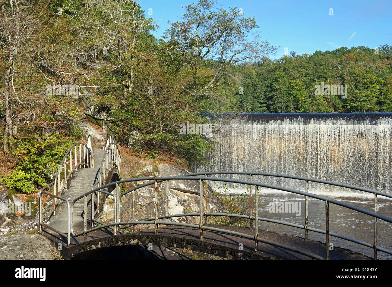 Curved footbridge over Glane river with waterfall dam in background ...