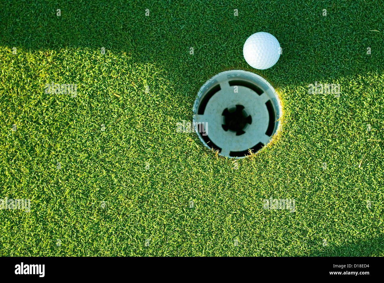 Golf ball in shadow next to golf green hole Stock Photo - Alamy