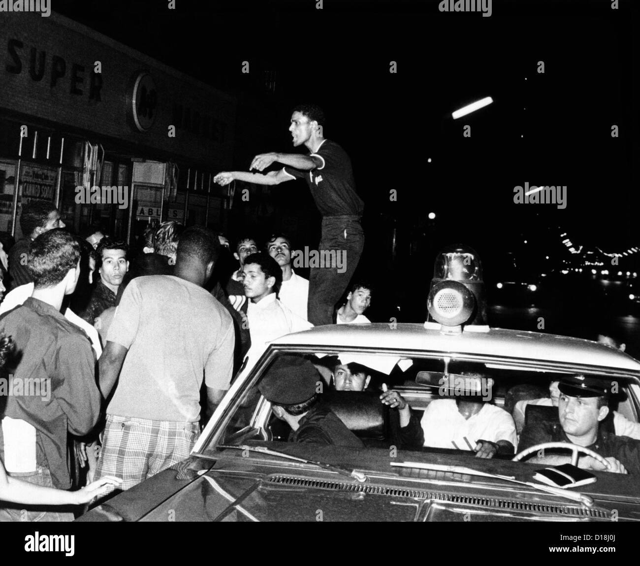Puerto Rican youth standing on a police car, urges the crowd to go home ...