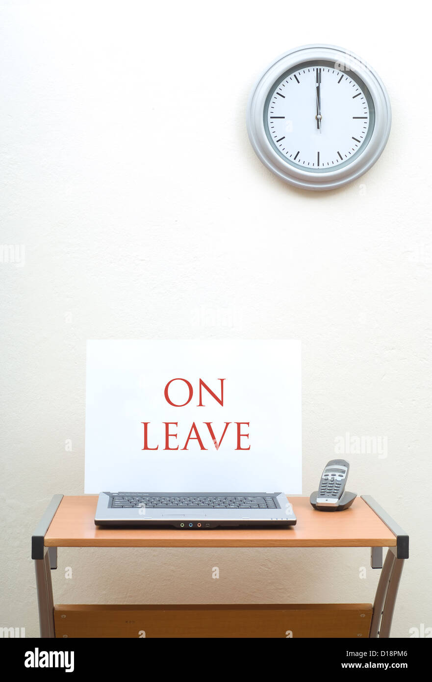 Office desk with on leave sign on open laptop with phone, clock on wall ...