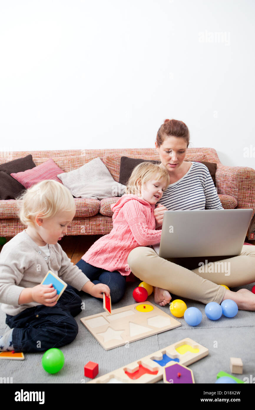 Mother using laptop, children playing Stock Photo - Alamy