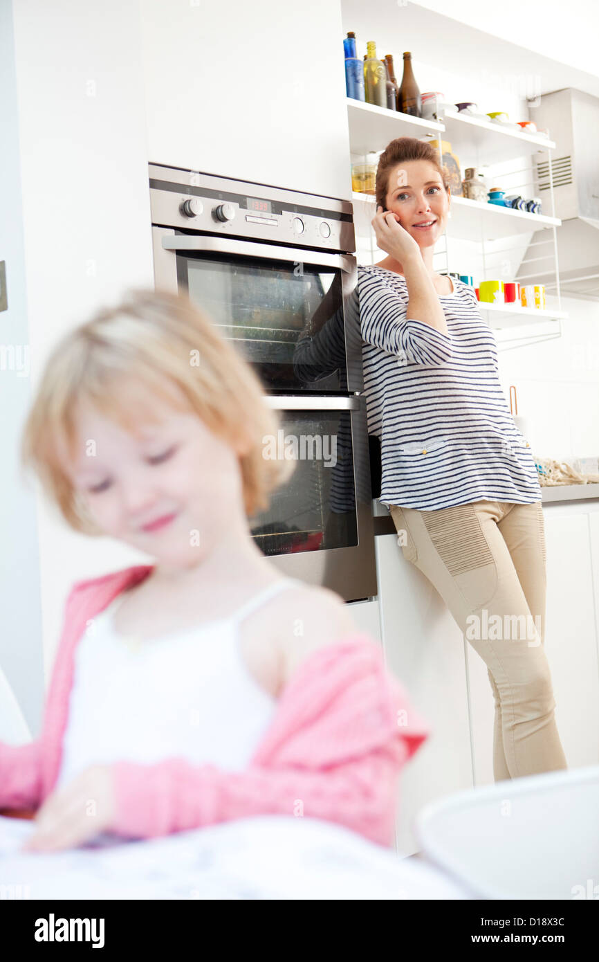 Mother on cell phone in kitchen with daughter in foreground Stock Photo ...