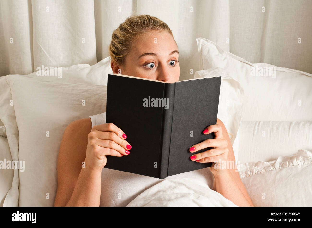 Surprised woman reading book in bed Stock Photo - Alamy