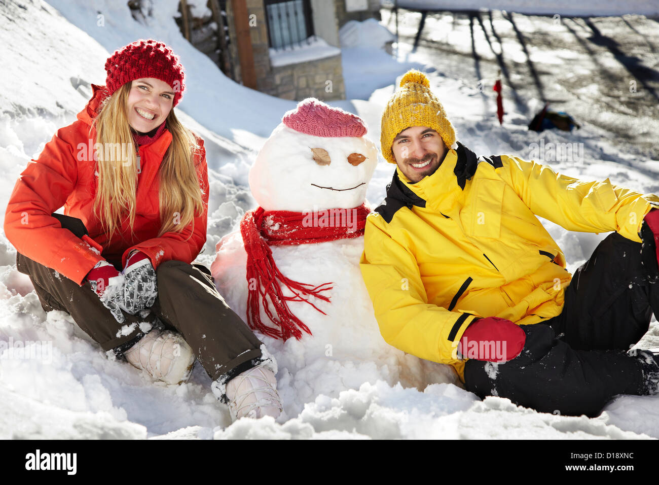 Couple sitting by snowman Stock Photo - Alamy