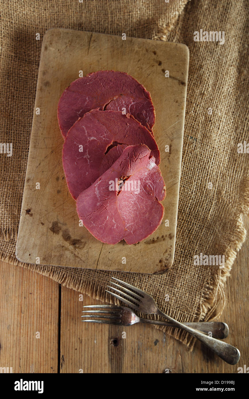 pastrami red meat slices on wooden table with hessian and forks Stock ...