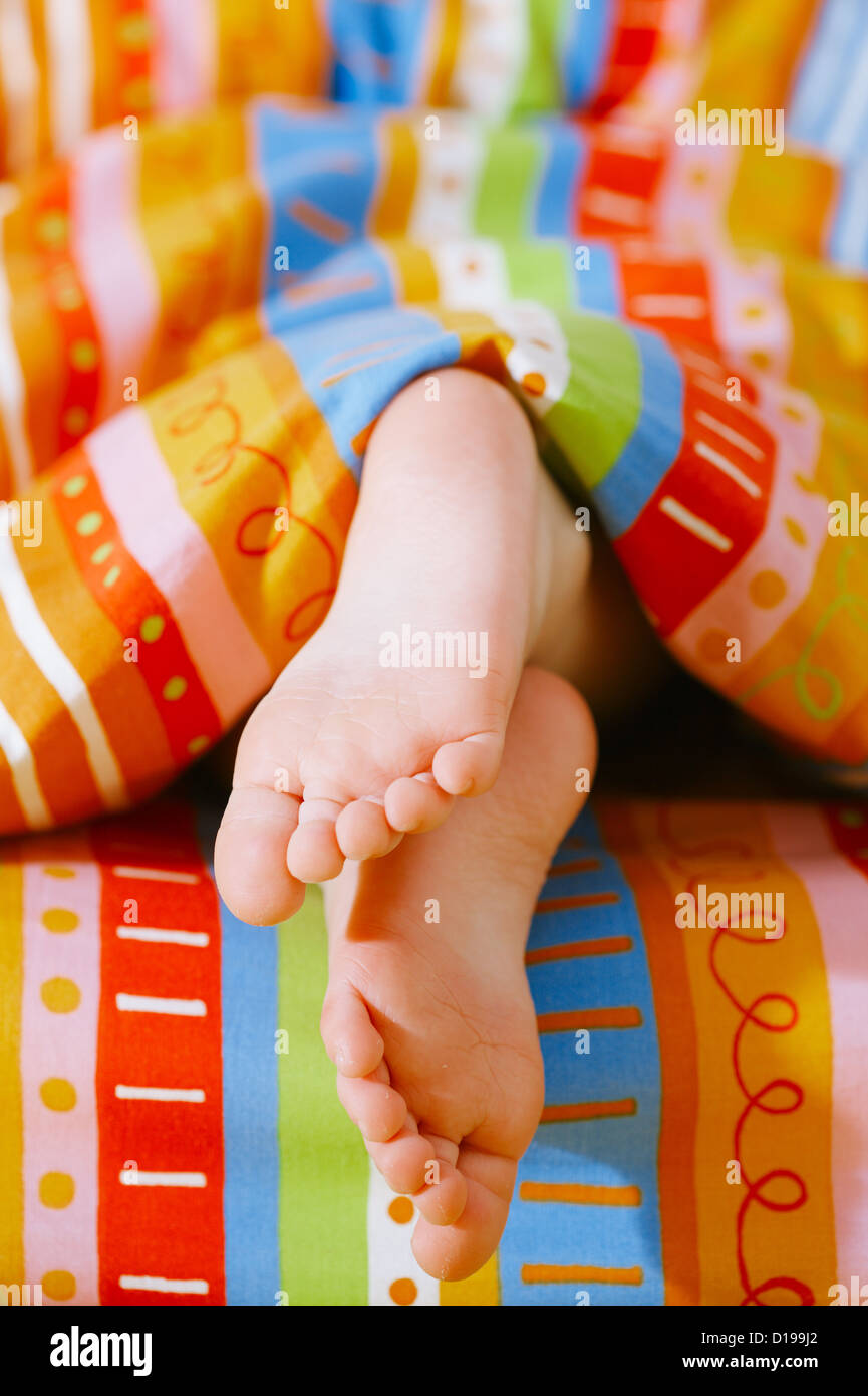 toddlers girl feet in a bed with colorful duvet under the morning sun ...