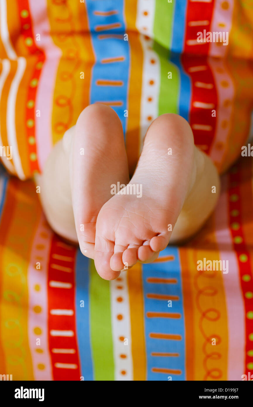 toddlers girl feet in a bed with colorful duvet under the morning sun ...