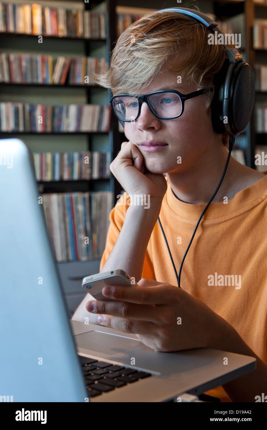 Pensive teenage school boy wearing headphones using Apple iPhone ...