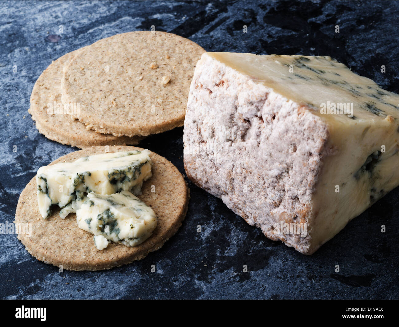 A piece of blue Stilton cheese with oat biscuits on a marbled slate ...