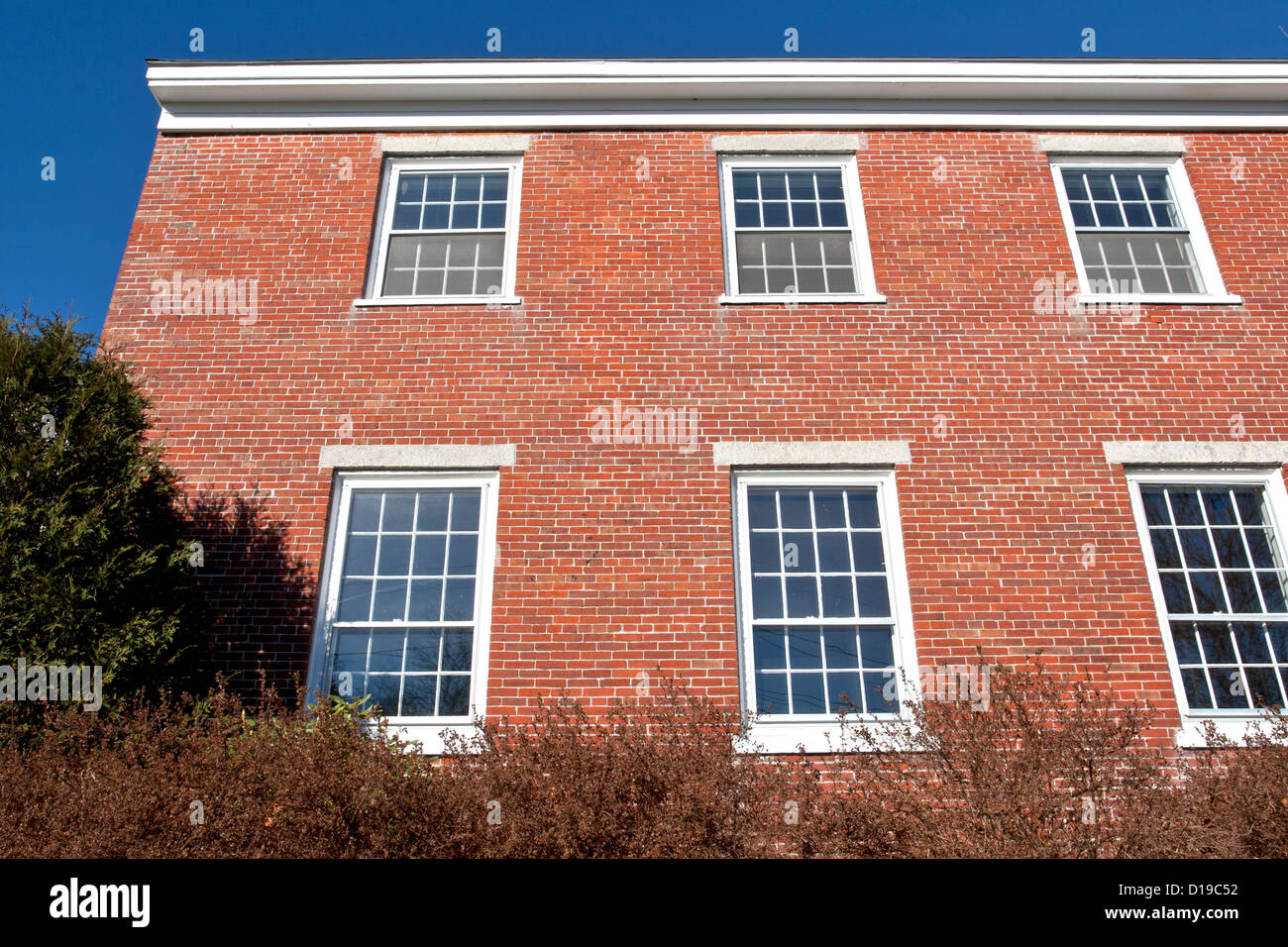 The exterior of an old brick building with white windows and foliage in ...