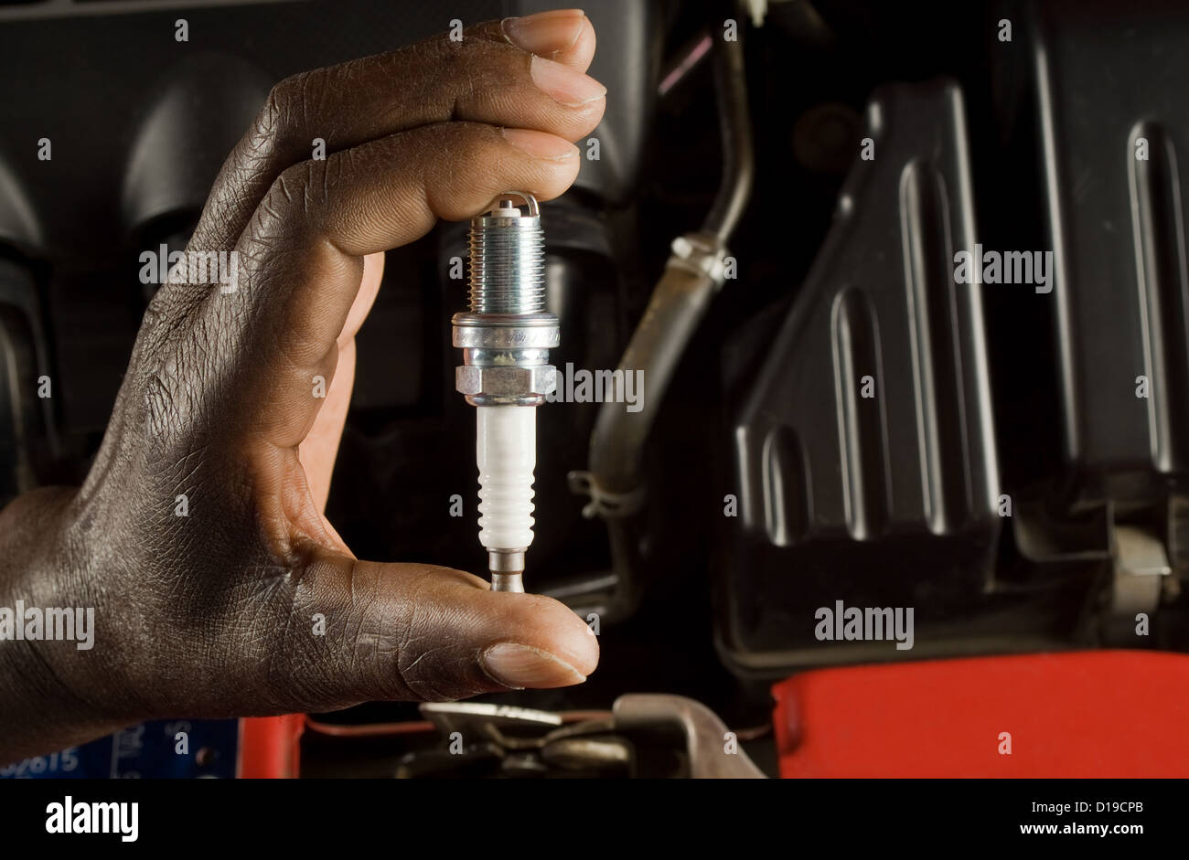 South African or American hand holding car spark plug with modern car ...
