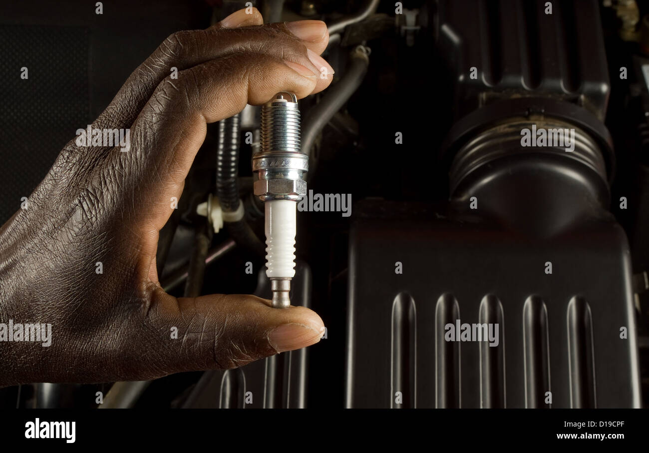 South African or American hand holding car spark plug with modern car ...