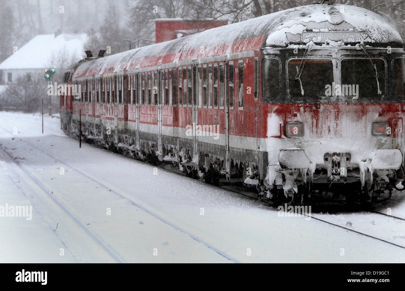 A regional express train is covered with snow and ice at the station in ...