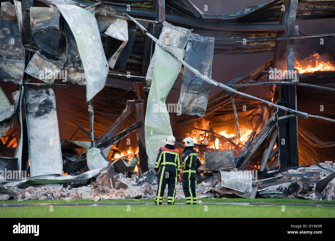 Two firefighters looking at a building that is detroyed by a huge fire ...