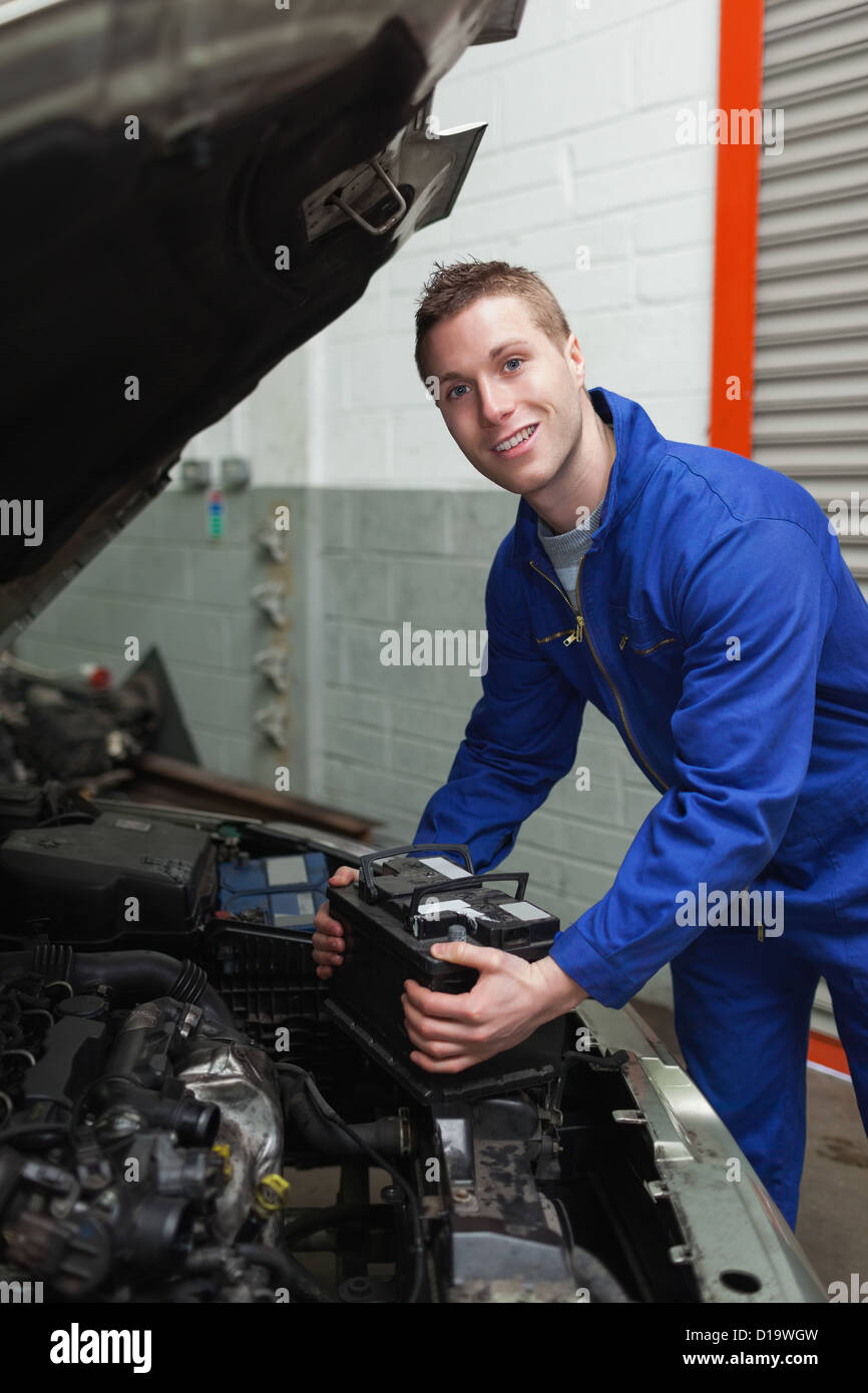 Happy mechanic with battery by car Stock Photo - Alamy