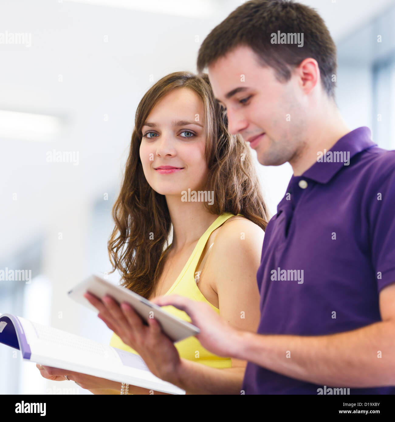 Two college students in library, reading books, using tablet computer ...