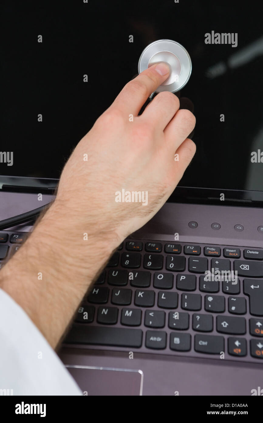 Hand examining laptop screen with stethoscope Stock Photo - Alamy