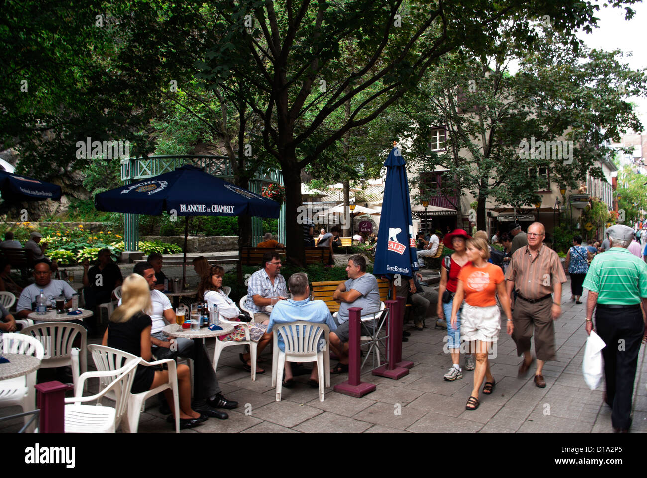 Tourists walk past garden patio where others are enjoying a cool drink ...