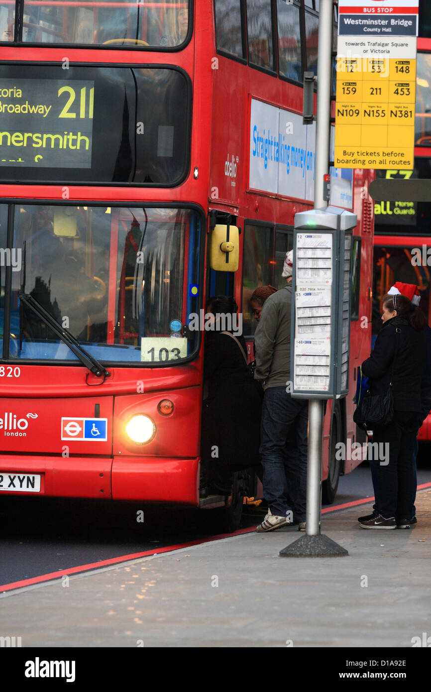 A queue of people boarding a red London bus at a bus stop Stock Photo ...