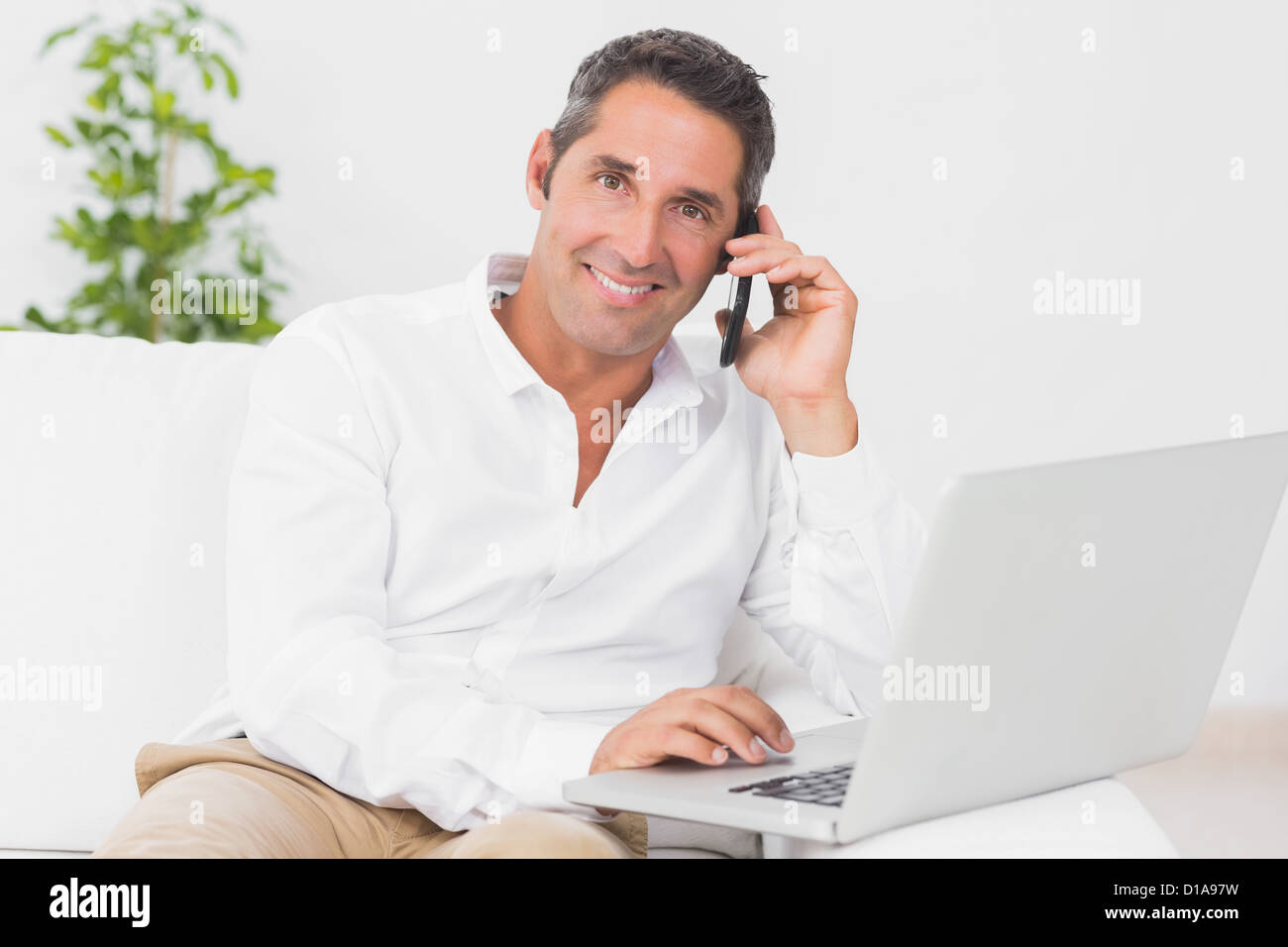 Smiling man using his laptop and phoning Stock Photo - Alamy