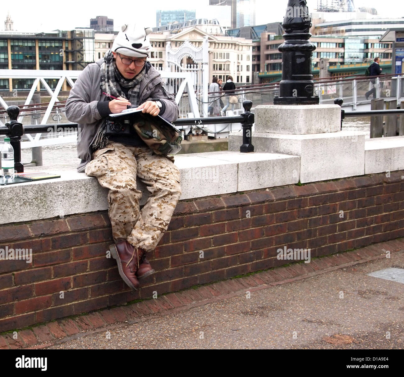 Artist with his sketch book sitting on the river wall in Bankside ...