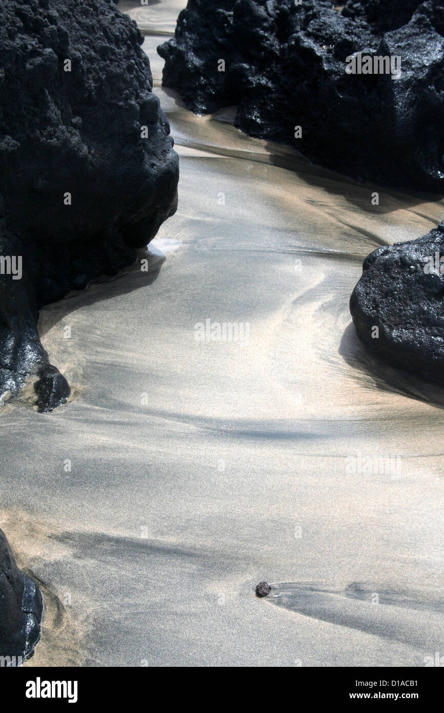 Black and golden sand mixing between lava rocks on Maui Island beach ...