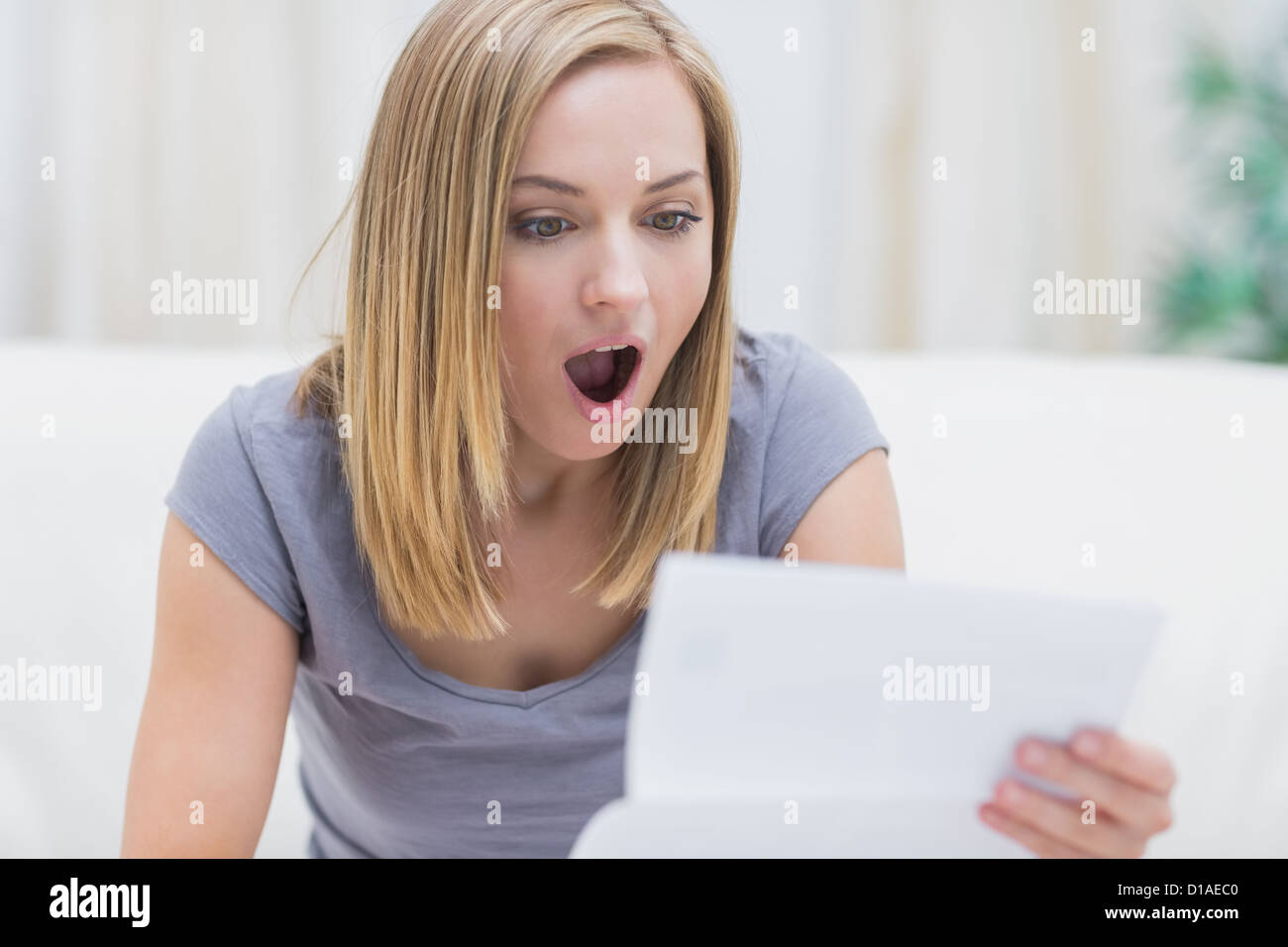 Shocked woman reading letter in living room Stock Photo - Alamy