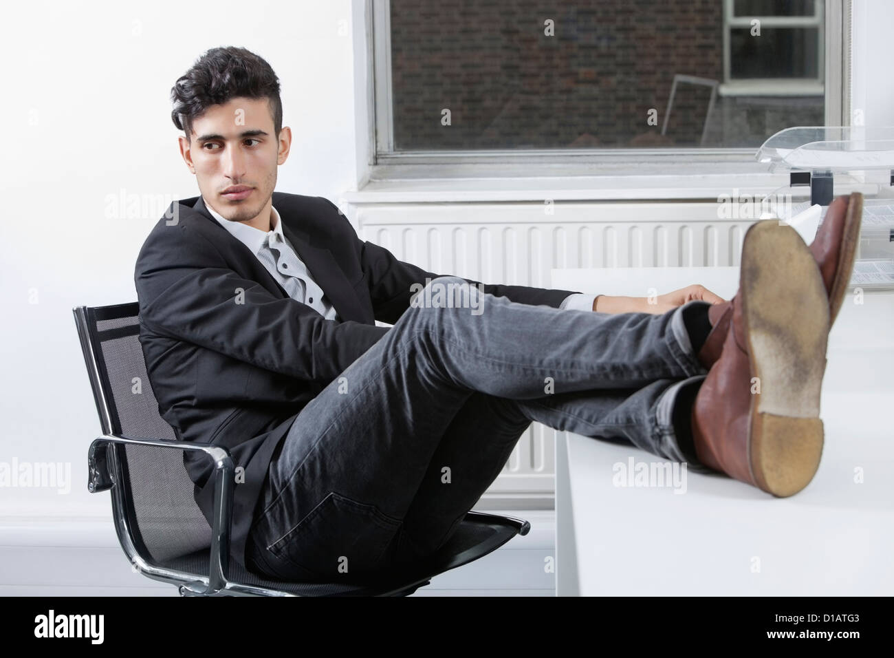 Thoughtful young businessman sitting legs raised at desk in office ...