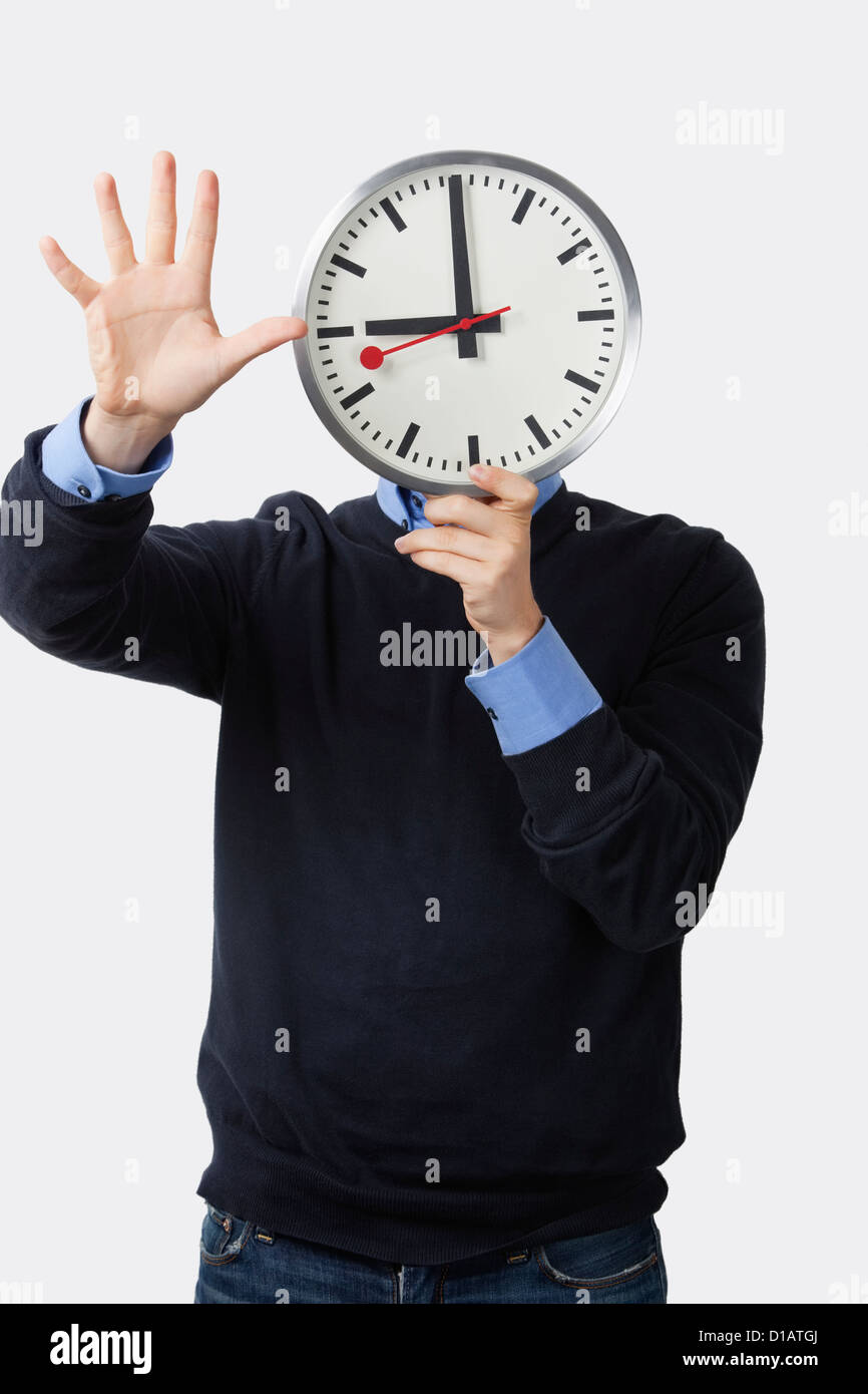 Young man holding clock over his face gesturing Stock Photo - Alamy
