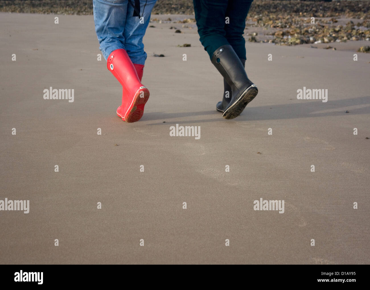 Two women walking along beach in winter, wearing wellies. Shot of ...