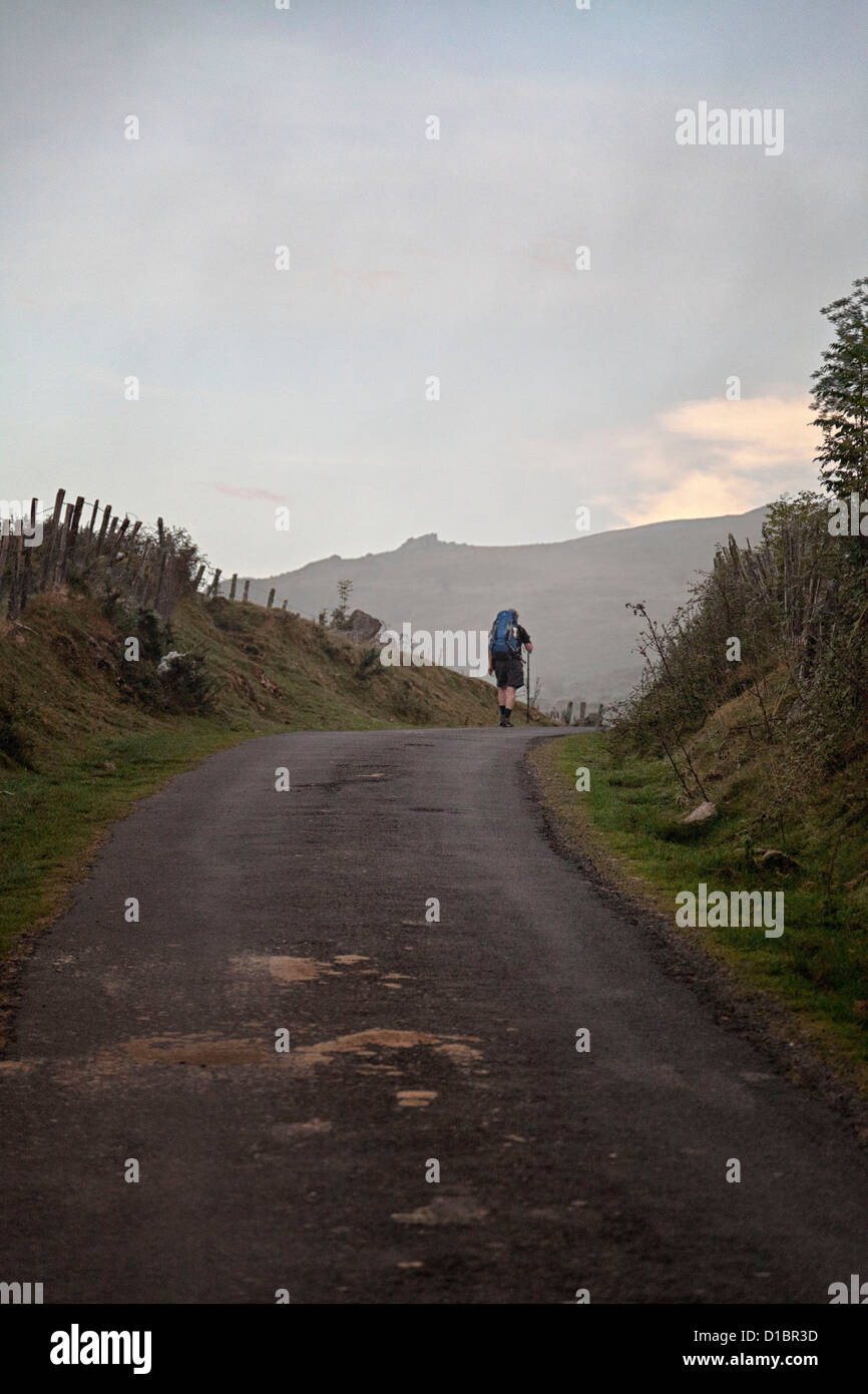 pilgrim walking a paved road in the Pyrenees, South France, between ...