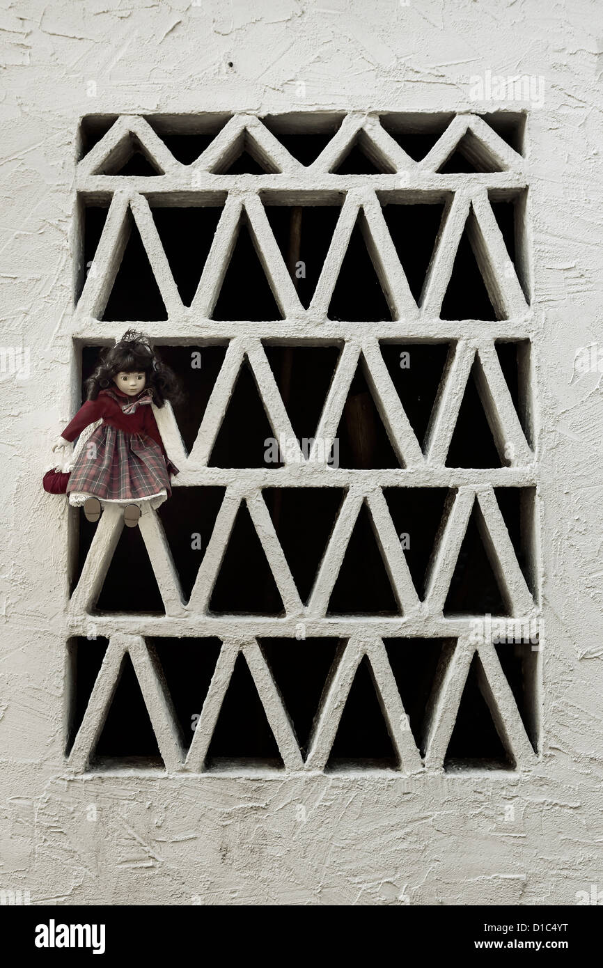 an old doll hanging on a window with a grate Stock Photo - Alamy