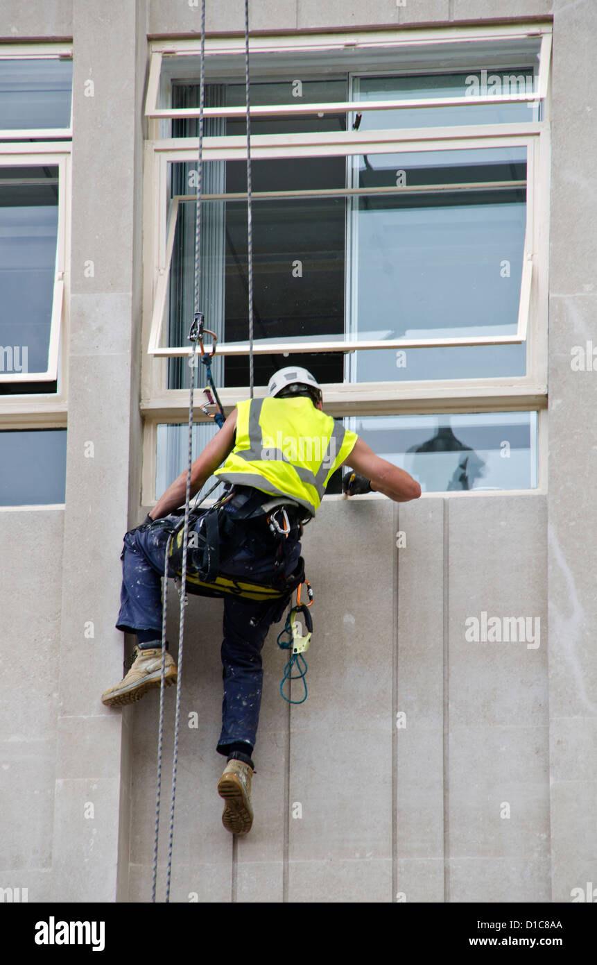 Worker hanging on the building`s unfinished window safely repairing the ...