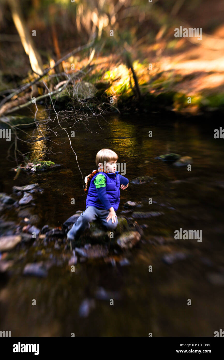 Little boy sitting on rock in the middle of a stream Stock Photo - Alamy