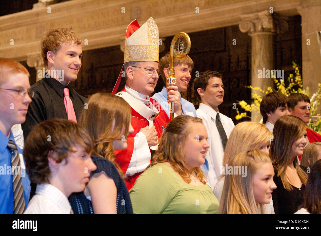 Priest wearing red vestments surrounded by teenagers during ...