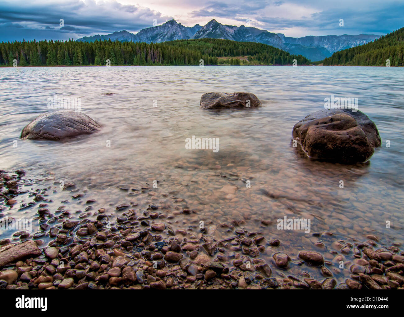 Three rocks in a ripply lake with forest and mountain peaks in the ...