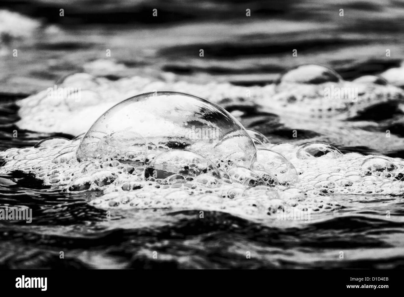 A bubble floats amidst foam on the surface of water beneath a waterfall ...