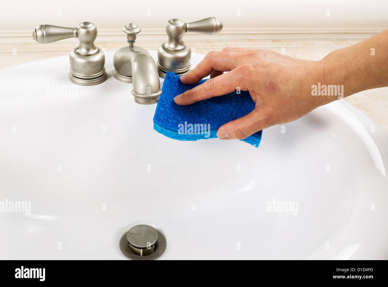 Hand with sponge cleaning bathroom sink faucet Stock Photo - Alamy