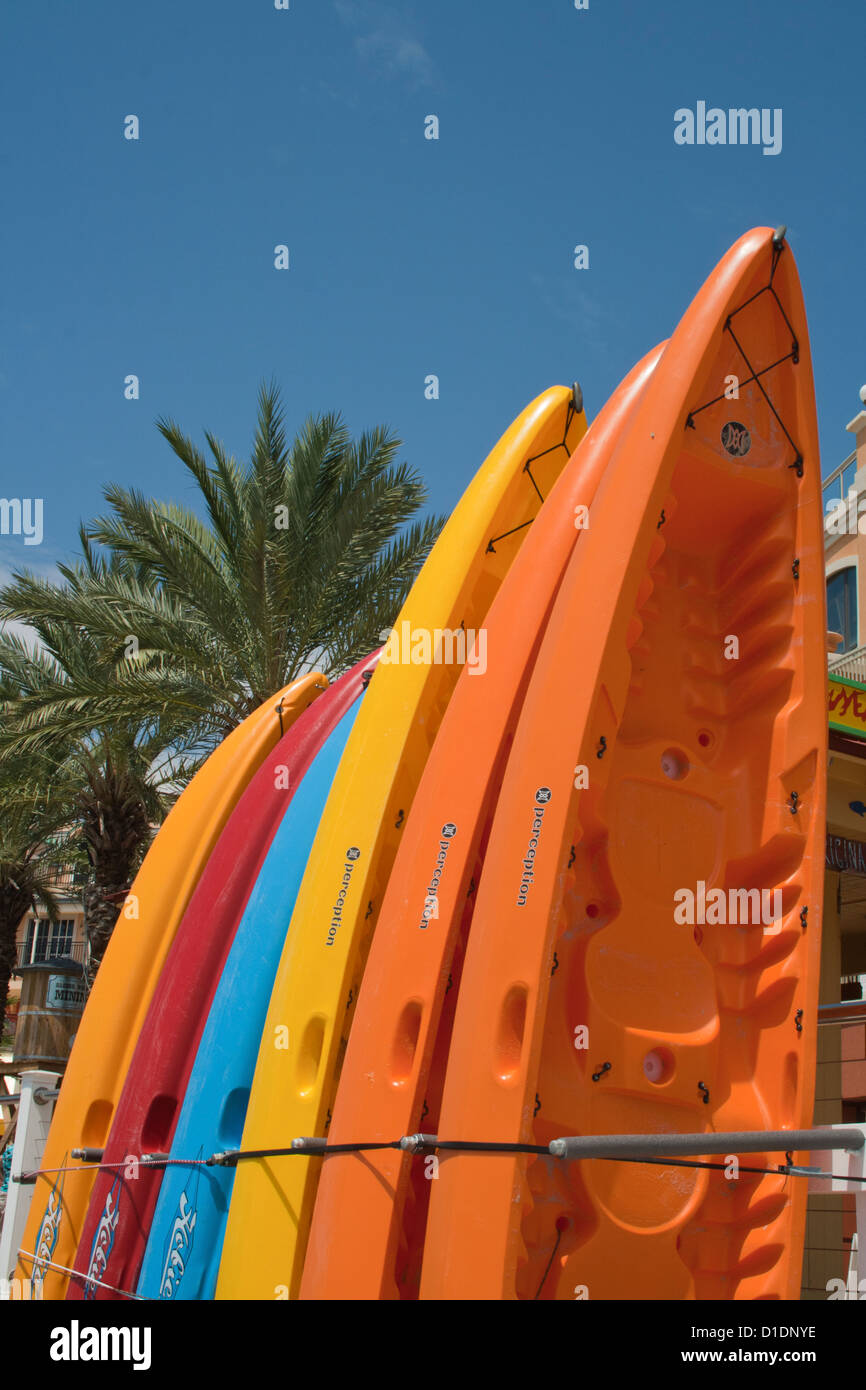 Kayaks stacked in colorful array against blue sky and green palm trees ...