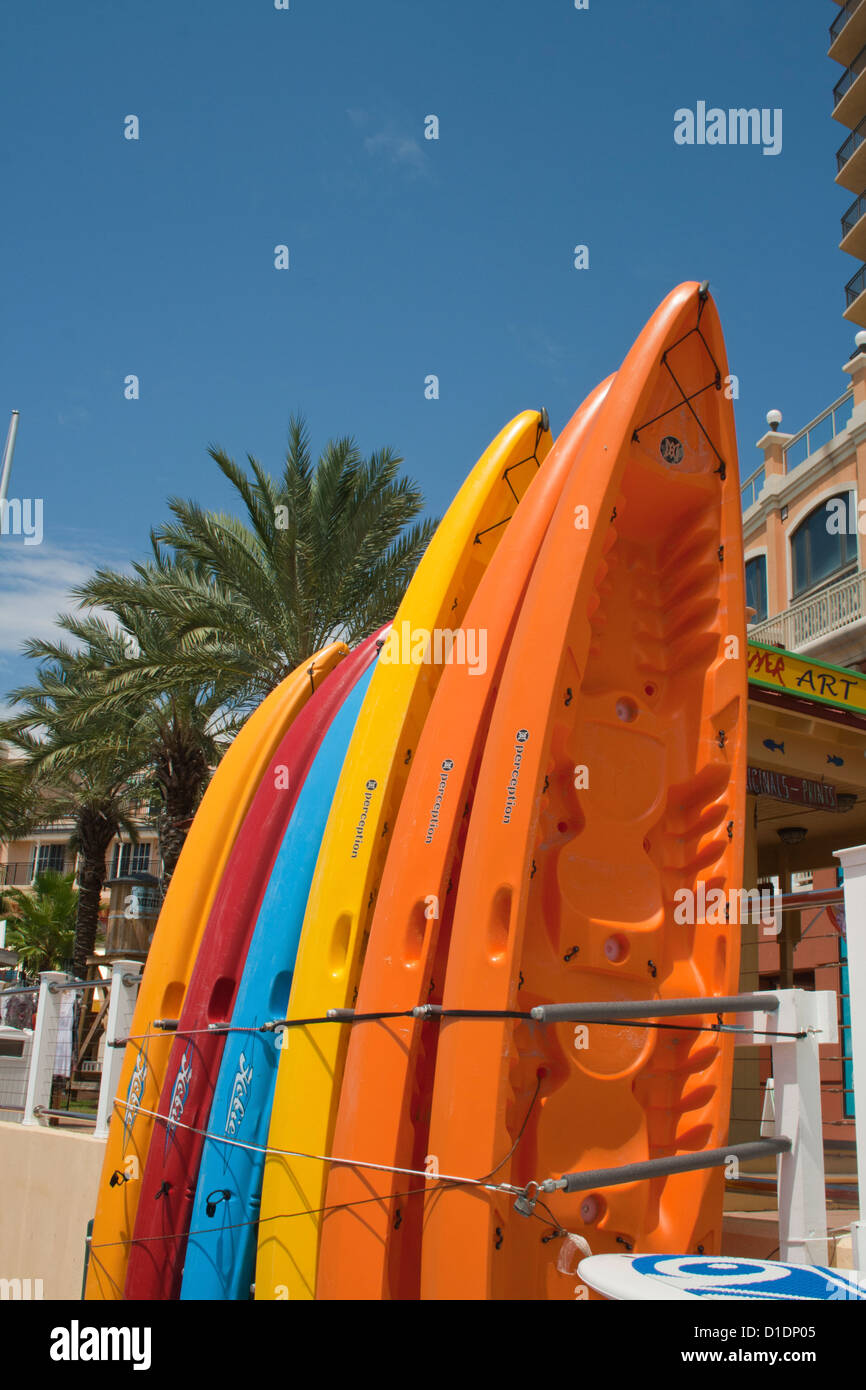 Kayaks stacked in colorful array against blue sky and green palm trees ...