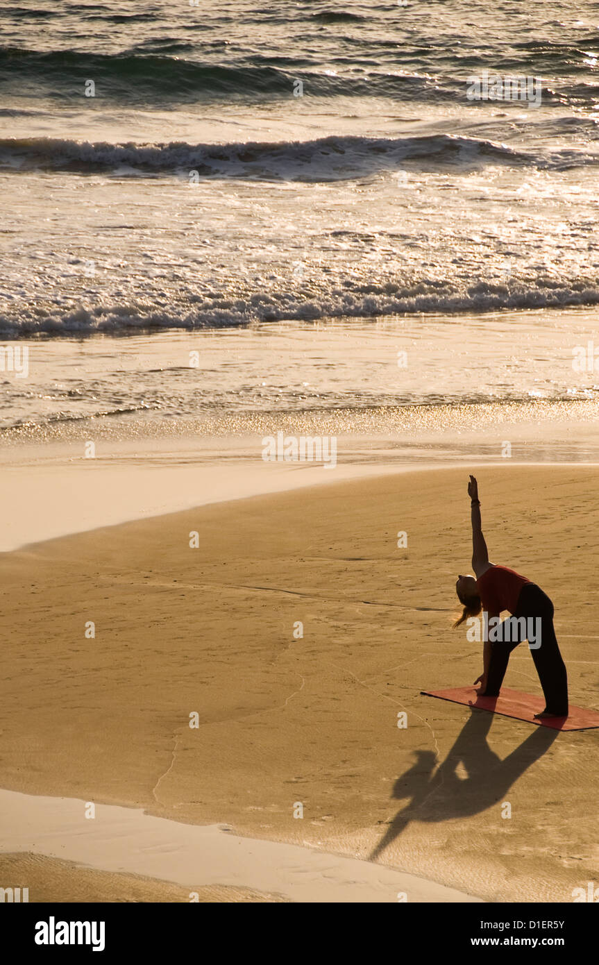 Vertical portrait of a lady practicing yoga on the beach at sunset in ...