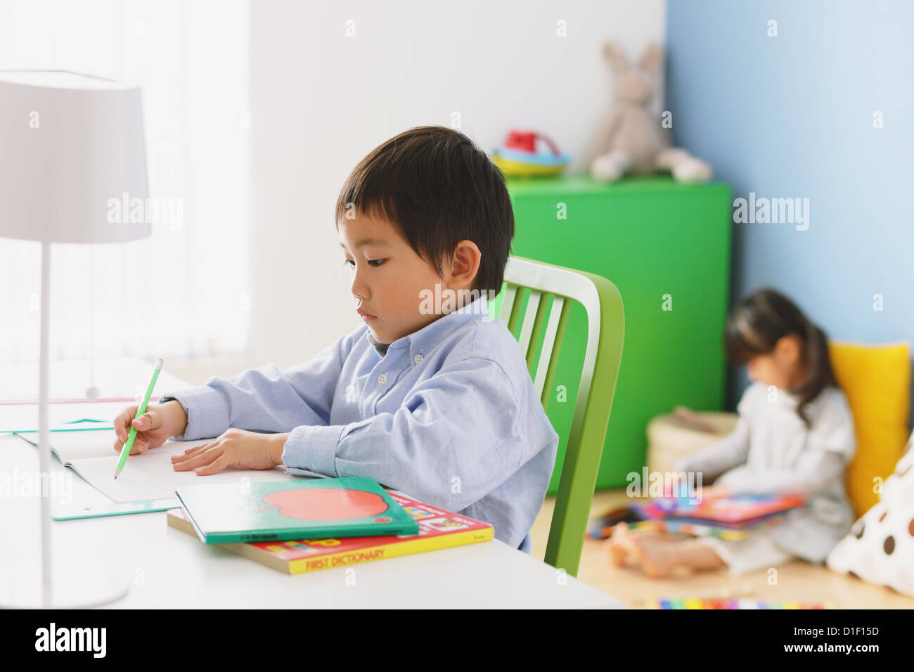 Elementary age boy doing his homework at his desk with his sister ...