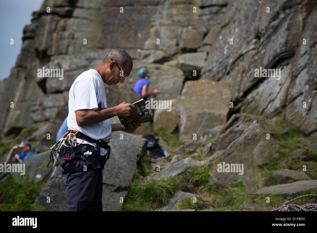 Male reading a rock climbing book /guide standing below Stanage edge in ...
