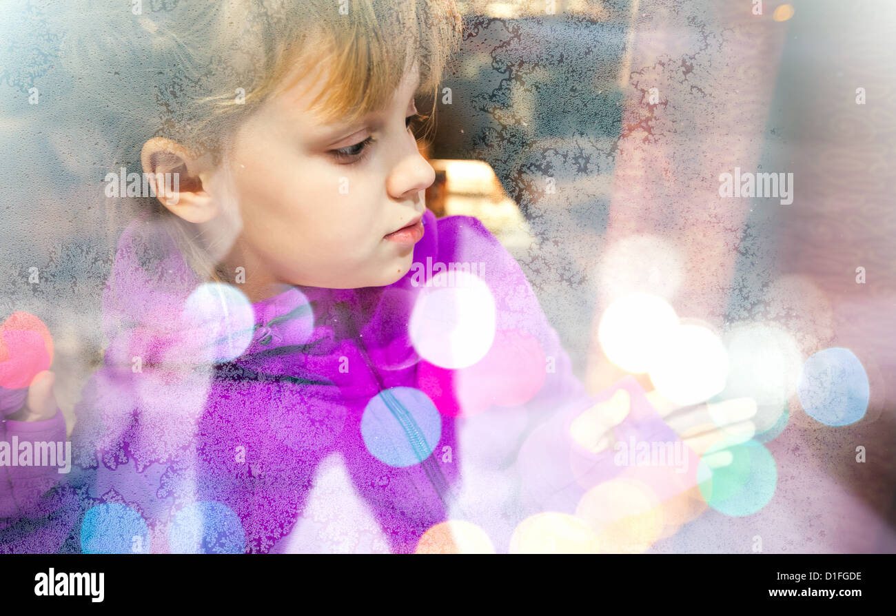 Little blond girl beyond frozen shop window glass with colorful blurred ...